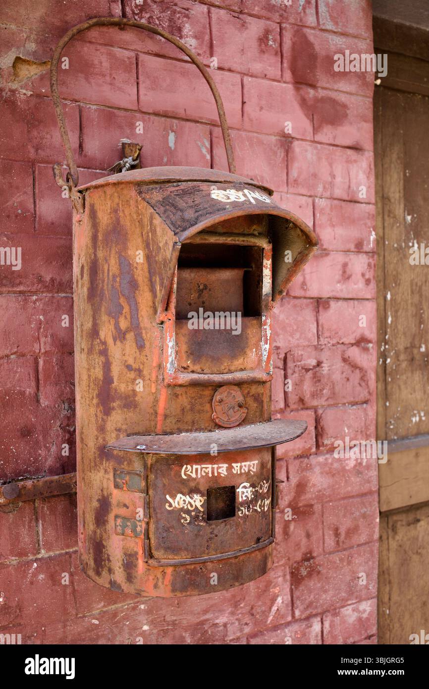 A rusted public letterbox with Bengali script, mounted on a red brick ...