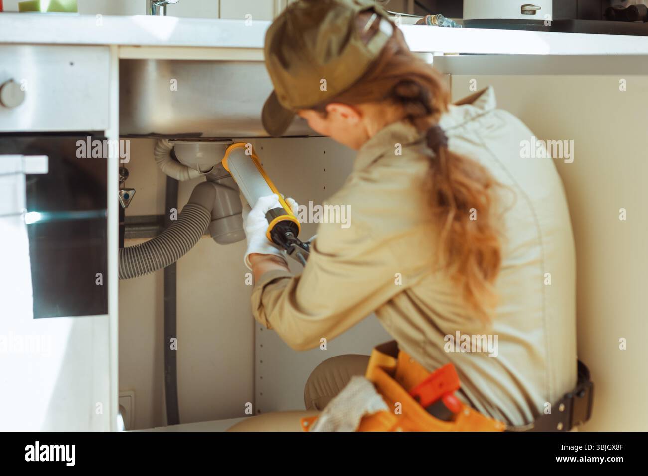 A skilled plumber with red hair uses a caulking gun to seal drain pipes ...