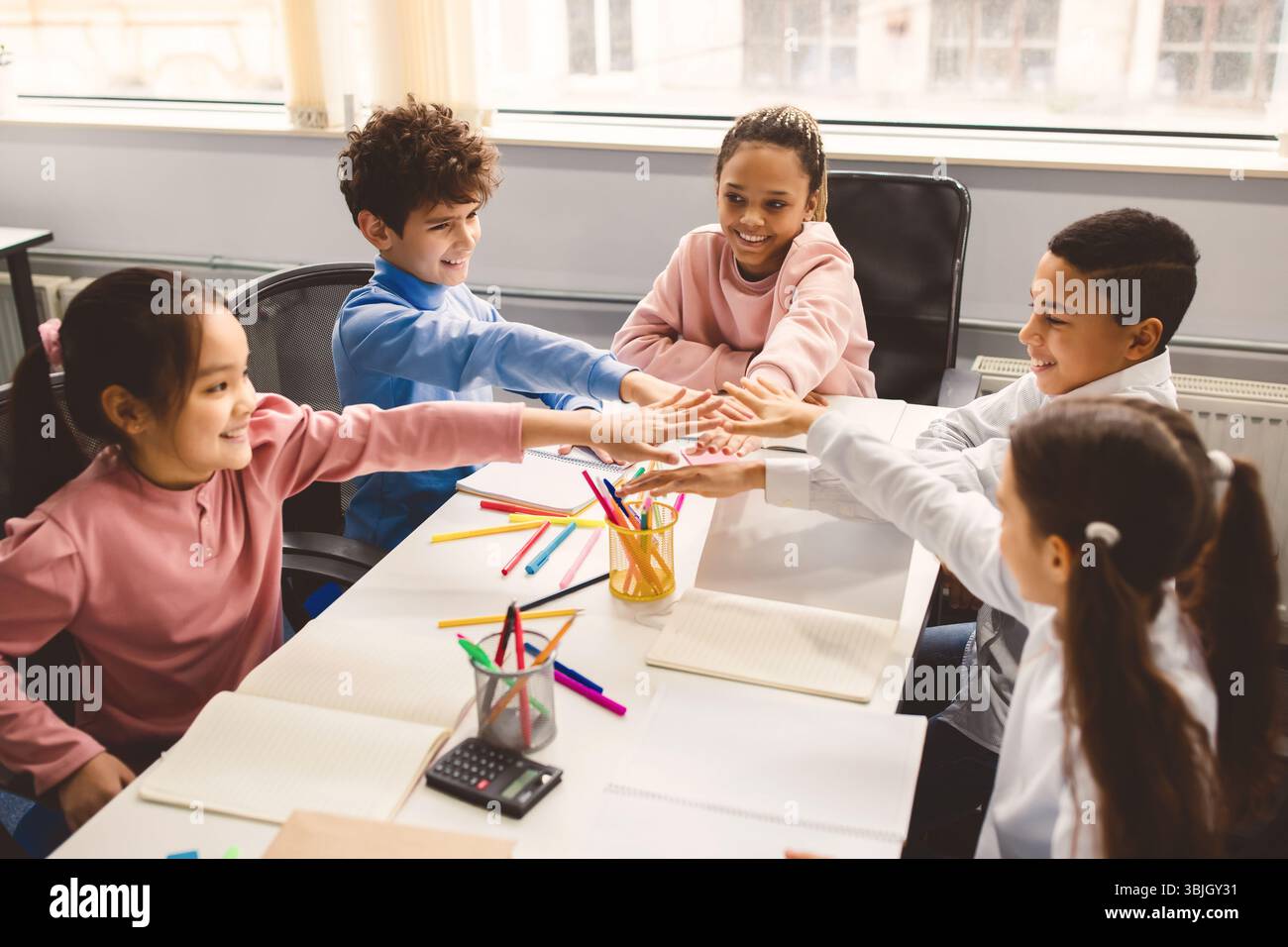 Happy diverse schoolchildren putting hands together at classroom Stock ...