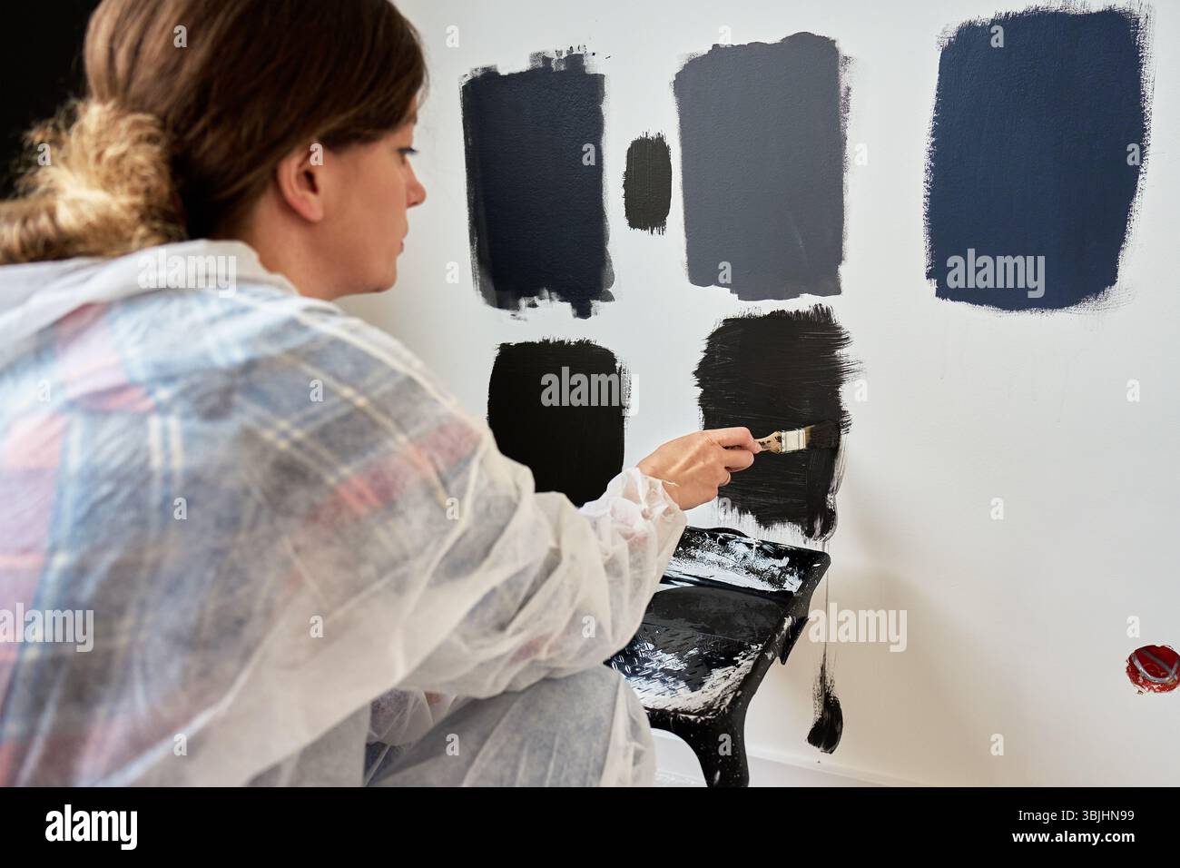 Woman in protective wear applies different dark paint swatches on white ...