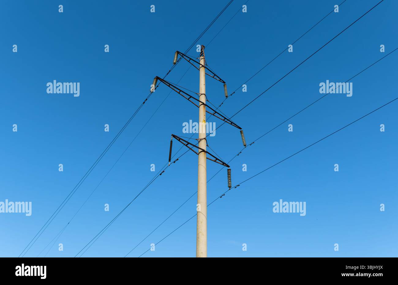 The top part of a tall power pole with wires and insulators against a ...