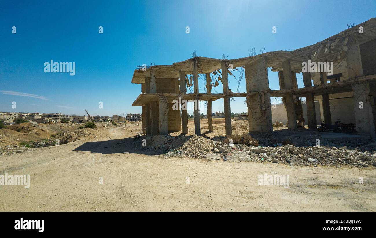 A partially destroyed concrete building stands in a barren, sandy ...