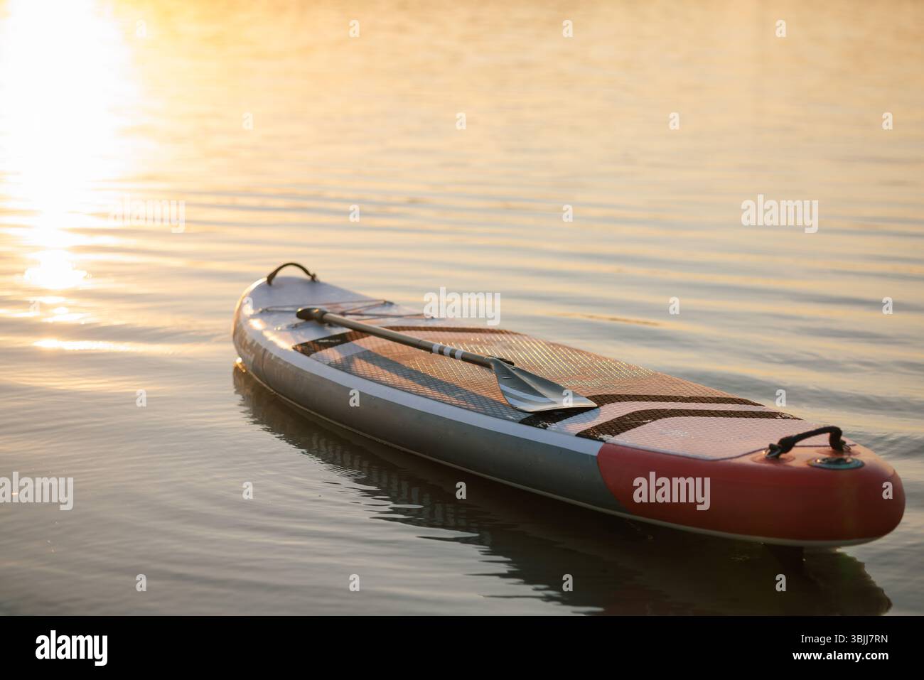 Inflatable paddleboard with paddle on still water at sunset ...