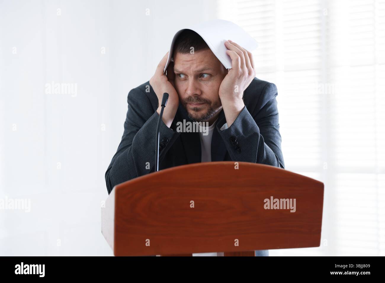 Fear of public speaking. Nervous man with microphone at lectern indoors ...