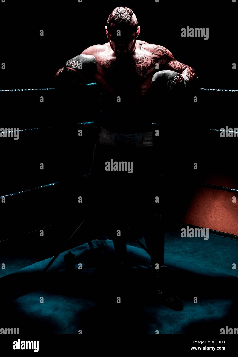 A male boxer stands in a boxing ring, illuminated by a spotlight. He is ...