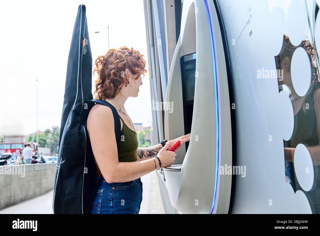 Young female musician withdrawing cash from a modern atm in an urban ...