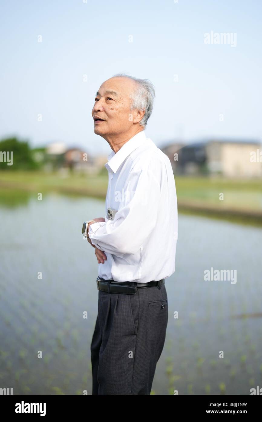 In rural Japan, a Japanese man in his late 70s walks along a farm road ...