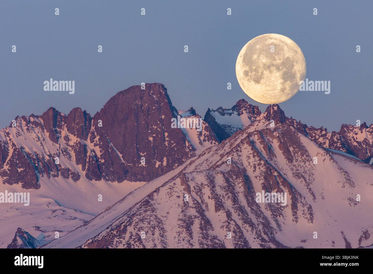 Dawn rises as the full moon sets on the snowy mountain peaks of the ...