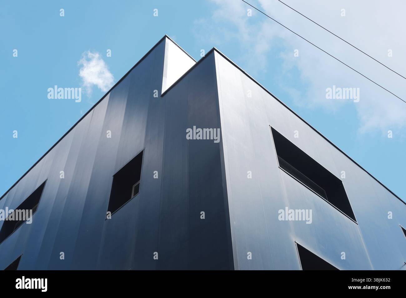 Sharp-edged black modern building with minimal windows against a bright ...