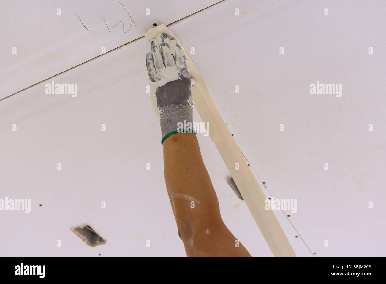 Carpenter is smoothing joint compound along ceiling seam using gloved ...