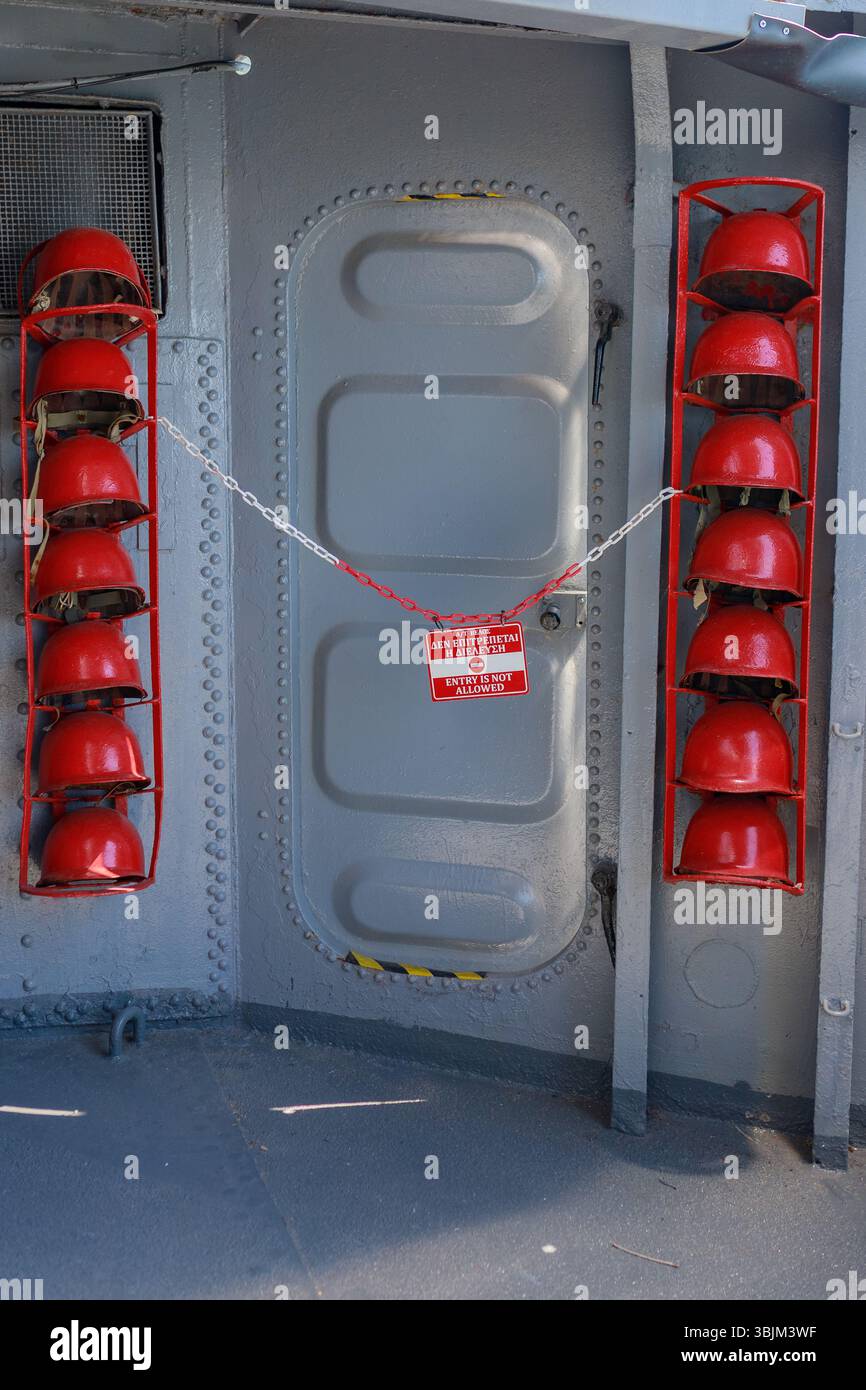 Gray ship door with chain barrier and stacked red helmets on military ...