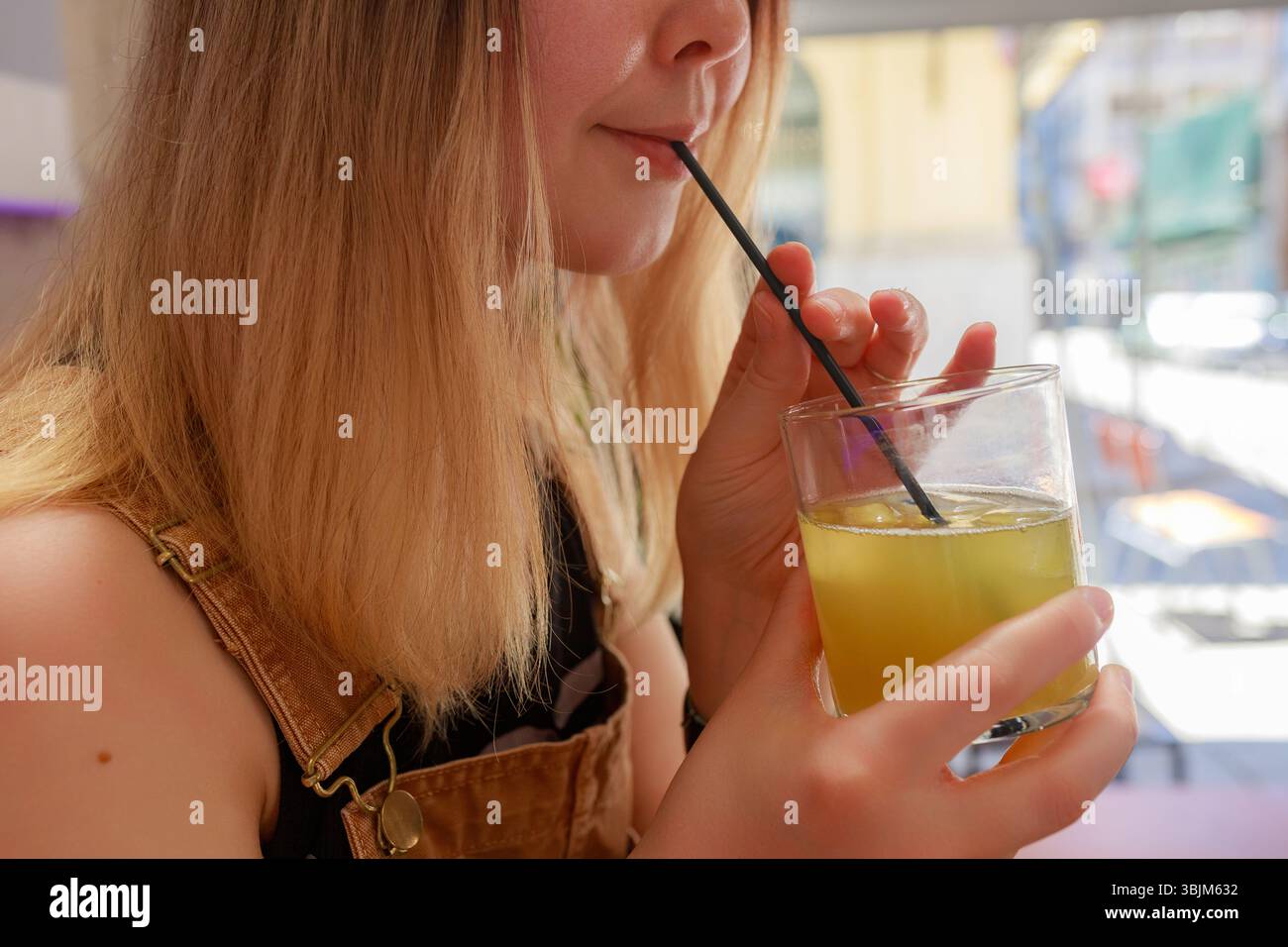 Close-up of woman’s hands and glass of iced citrus drink, sipping straw ...