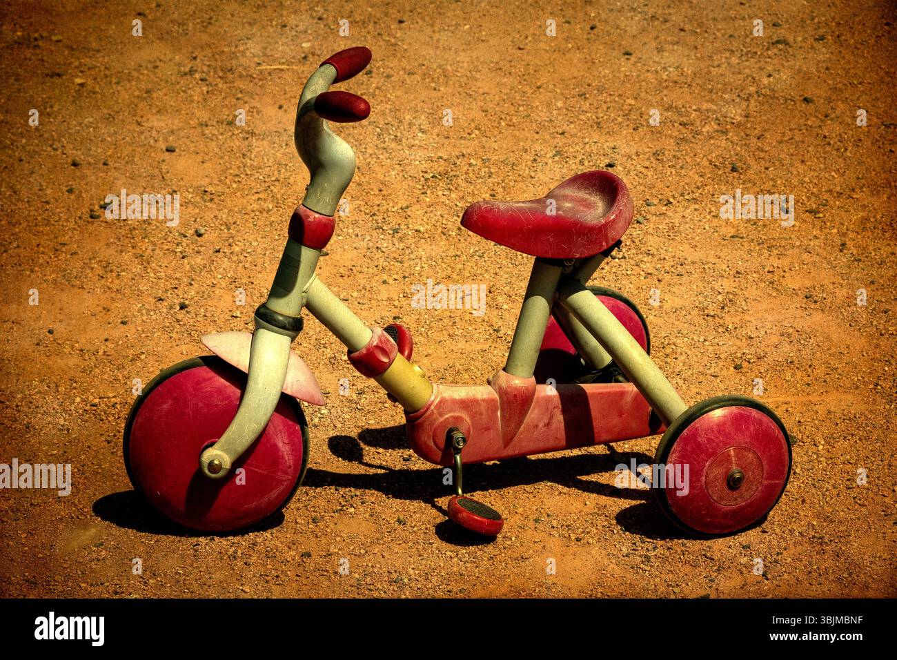 A vintage red tricycle sits abandoned on a sandy ground, showing signs ...