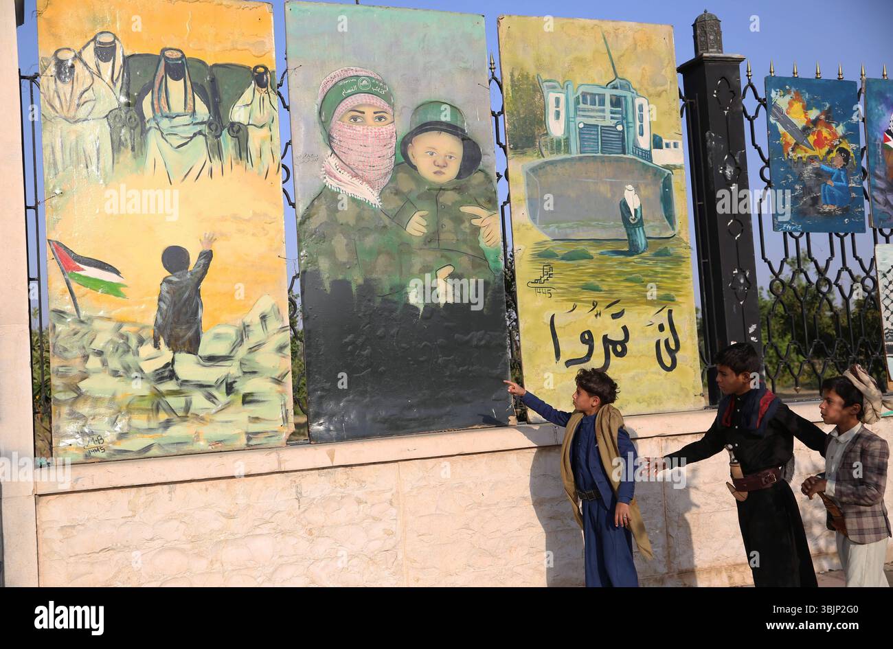 YEMEN SANA A DAILY LIFE - Boys walk past a fence adorned with pro ...