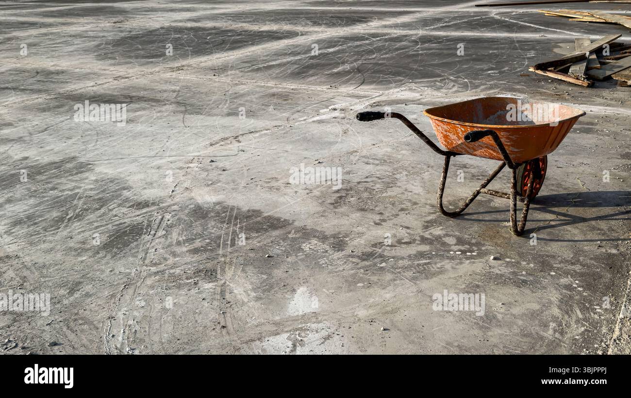Old orange construction wheelbarrow on textured concrete ground at ...