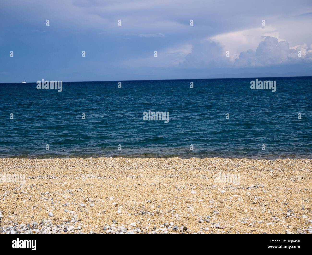 Coastal scene showing sandy beach and deep blue ocean beneath a lightly ...