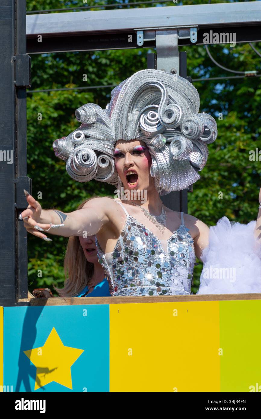 A drag queen in a silver sequin costume is performing on a parade float ...