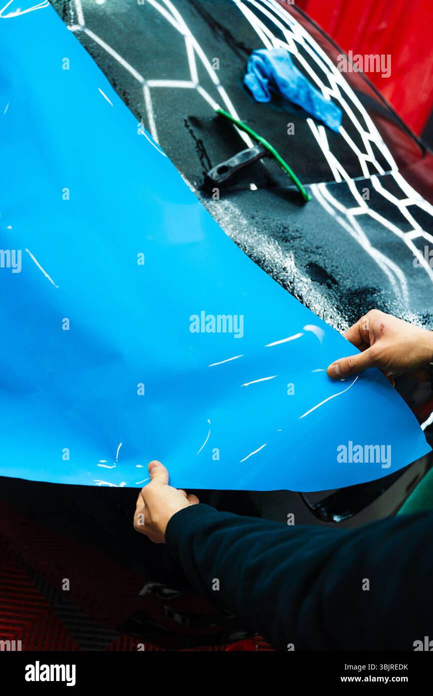 Applying PPF wrap on car during full detailing. Bold blue vinyl wrap ...