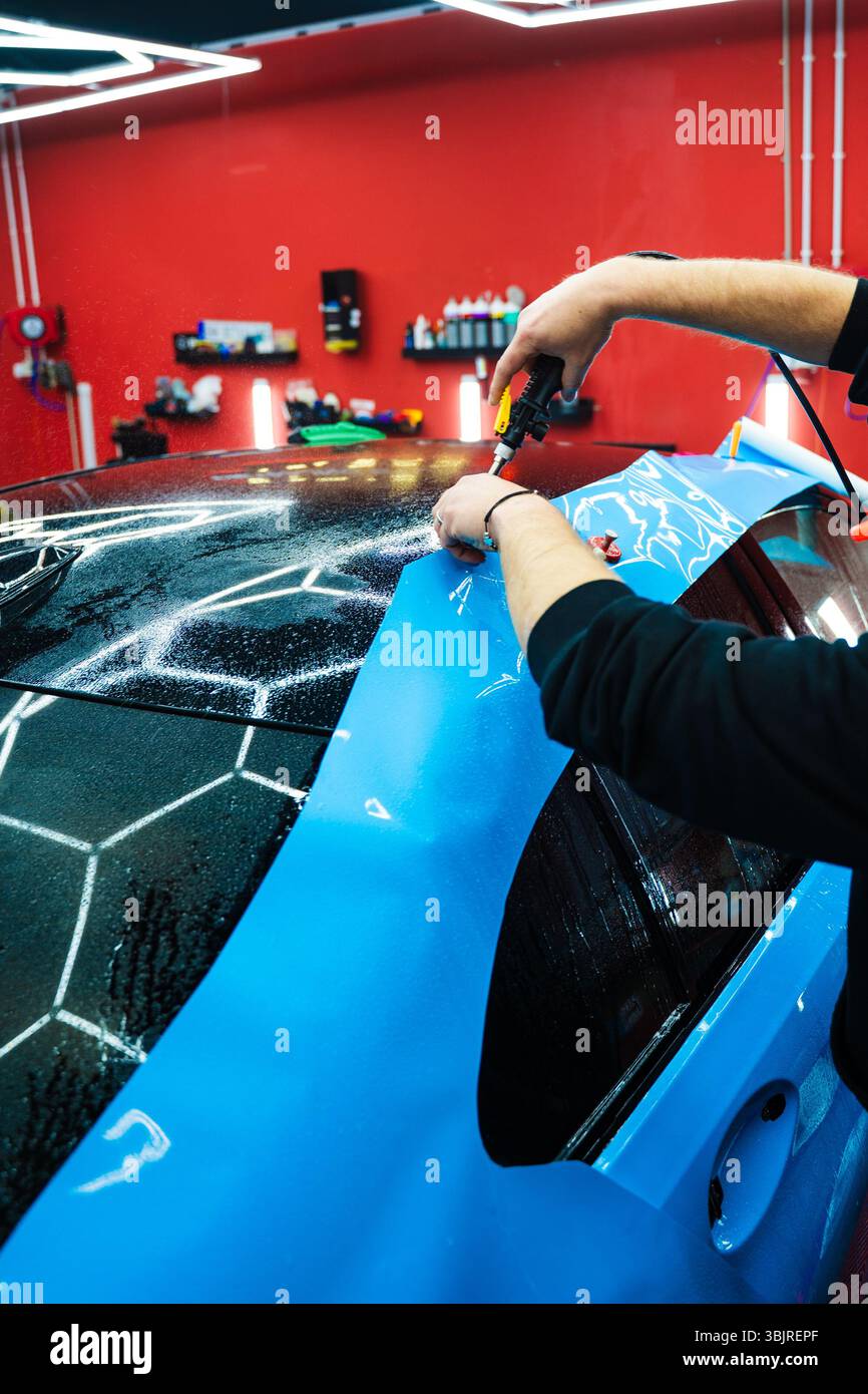 Applying PPF wrap on car during full detailing. Bold blue vinyl wrap ...