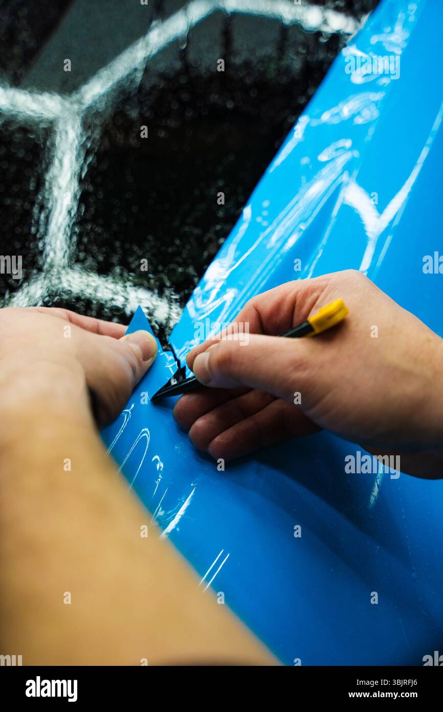 Detailing technician trims blue PPF on a car panel for perfect contour ...