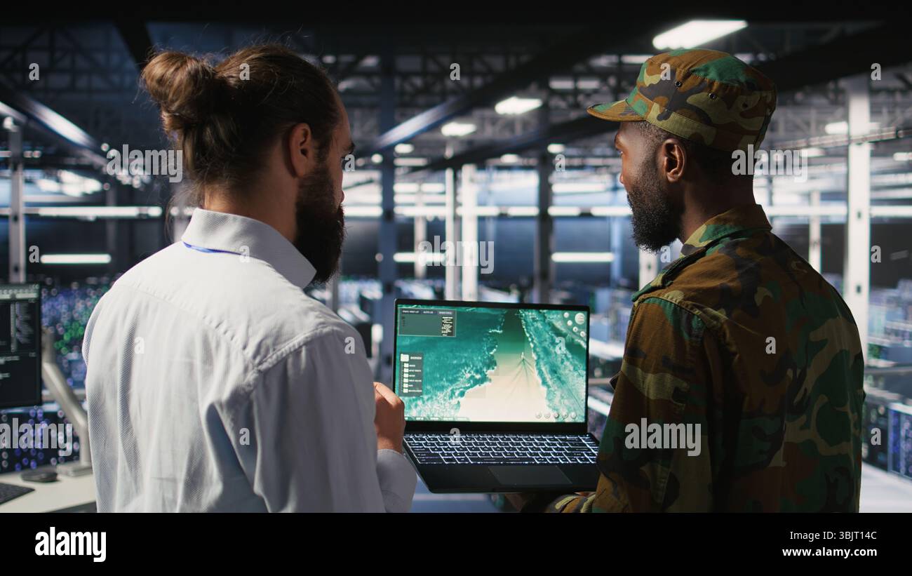 Drone operators in military data center supervising autonomous flight systems through laptop ...