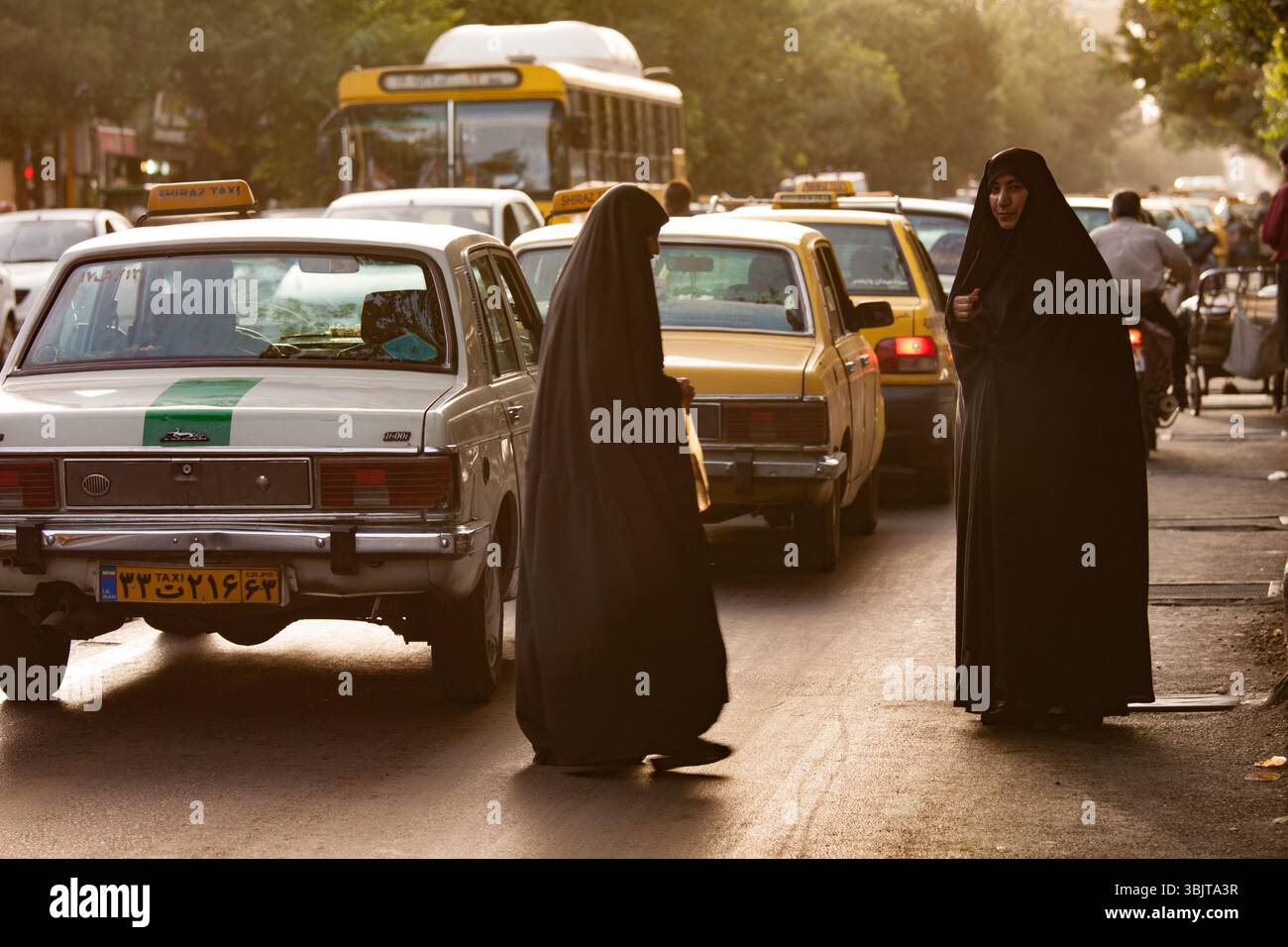 Busy street in Shiraz, Iran, with yellow taxis, city bus, and two women ...