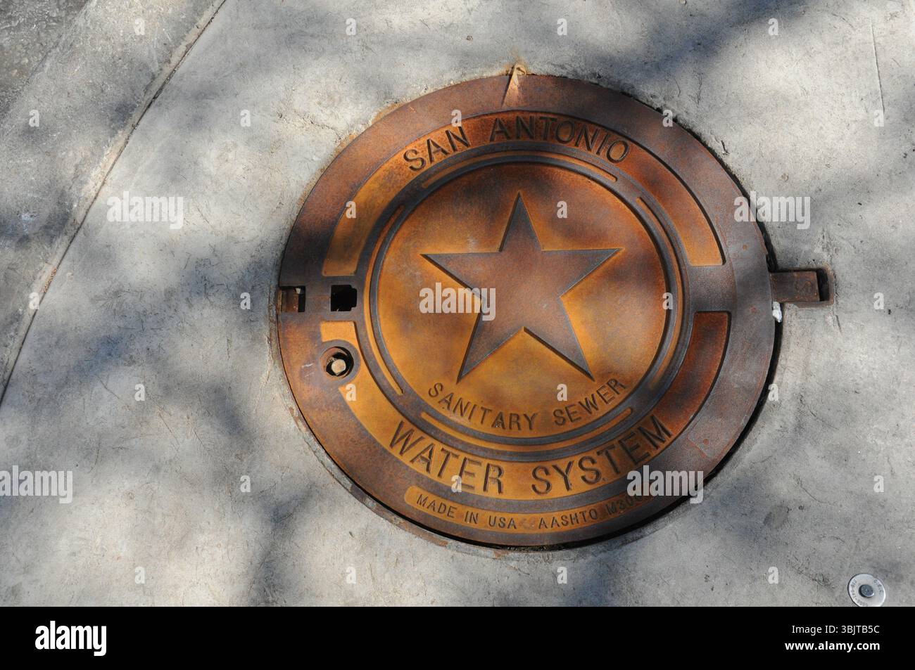 Rustic manhole cover of San Antonio Water System on a sunlit concrete ...