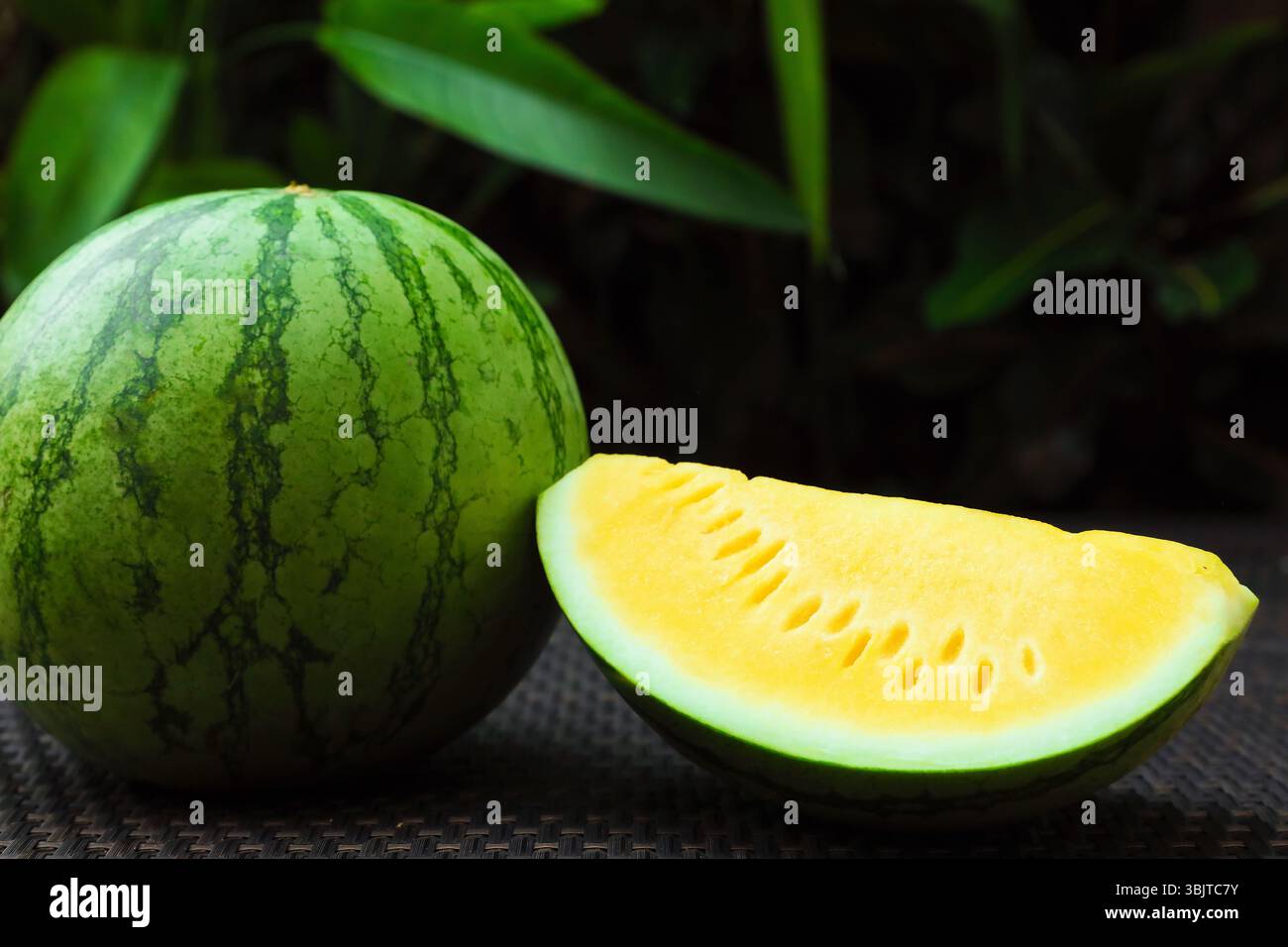 Whole and cut yellow watermelons on wicker table outdoors, closeup ...