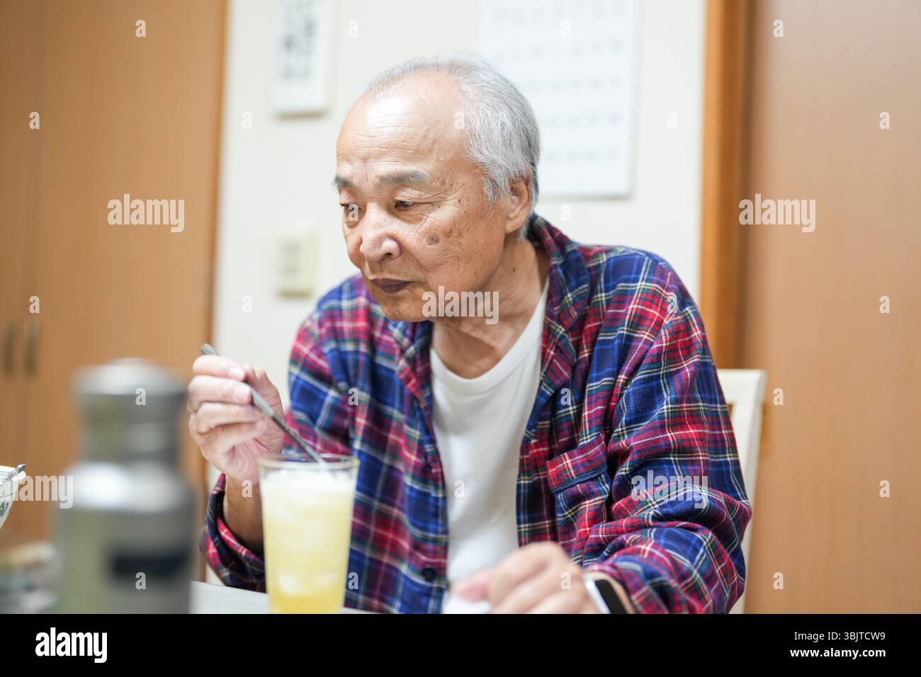 A Japanese man in his late 70s, wearing checkered pajamas, enjoys a ...