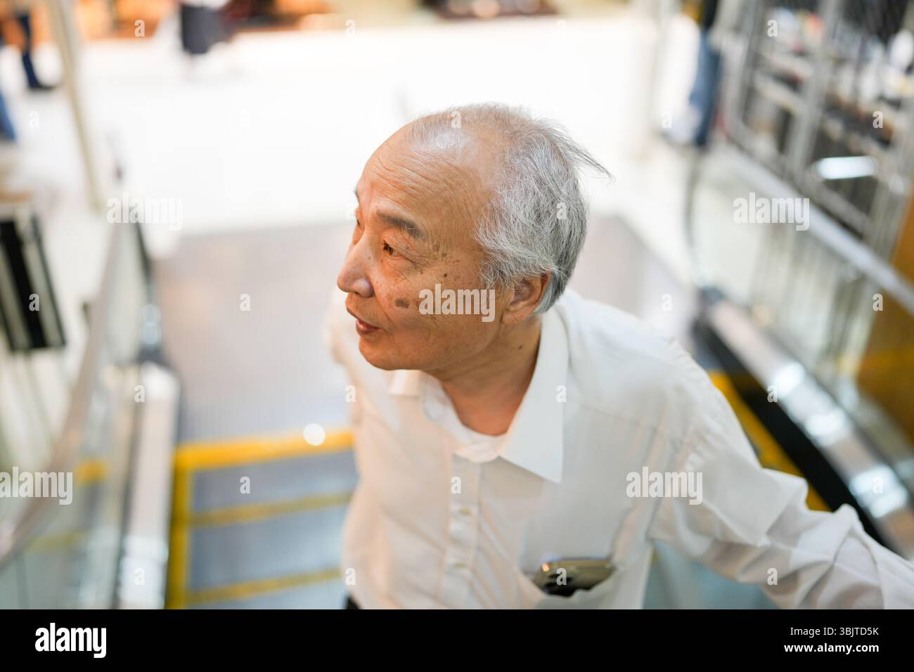 In an indoor escalator setting in Japan, a Japanese man in his late 70s ...