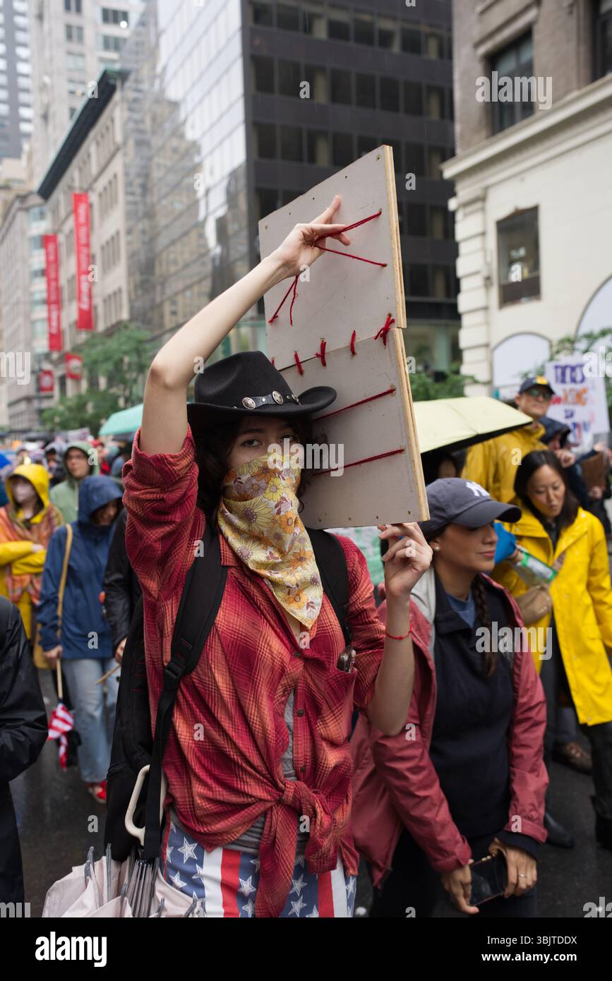 A young woman with a bandana and cowboy hat holds a rectangular sign ...