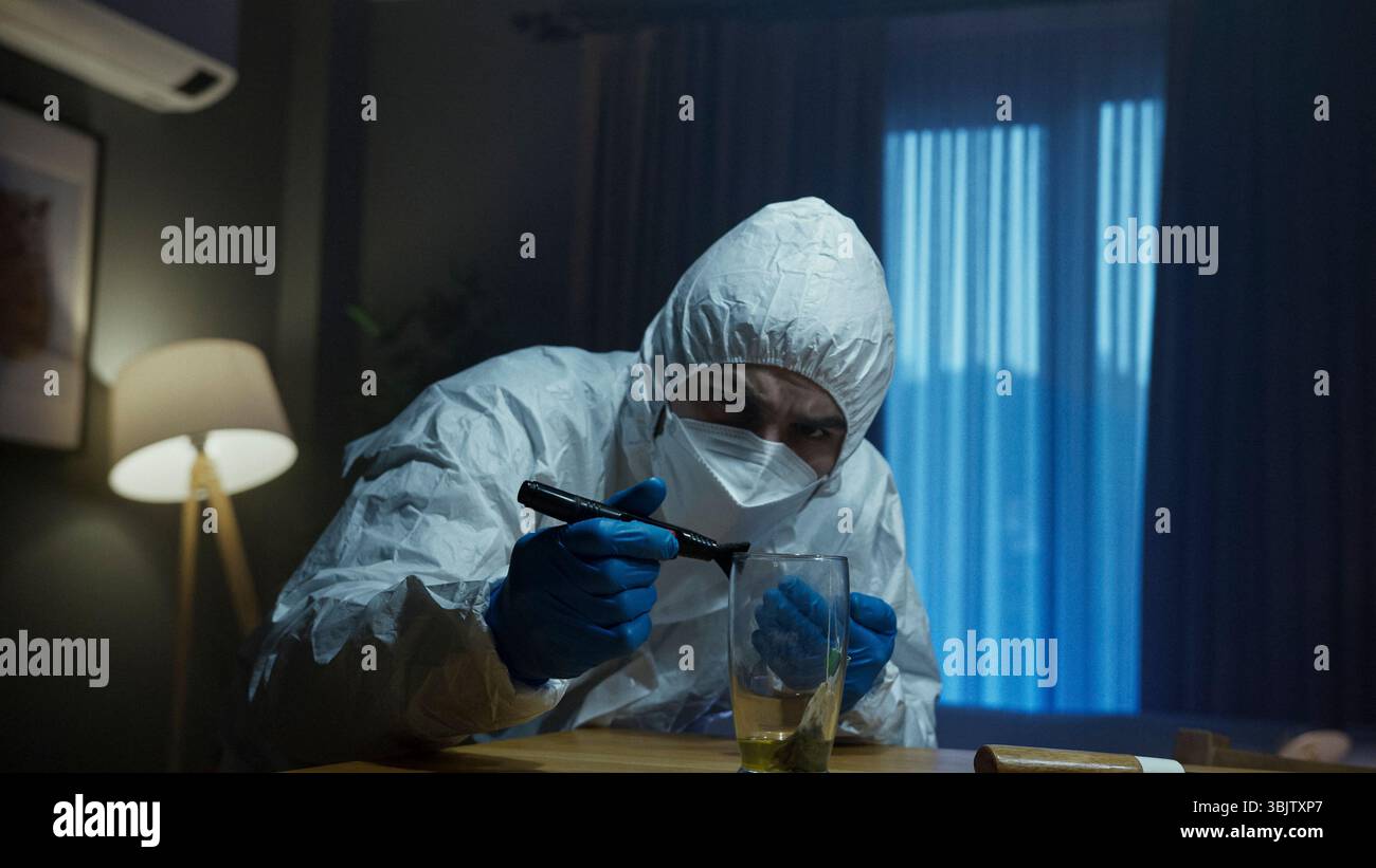 Investigator in hazmat suit examines a glass with UV flashlight ...