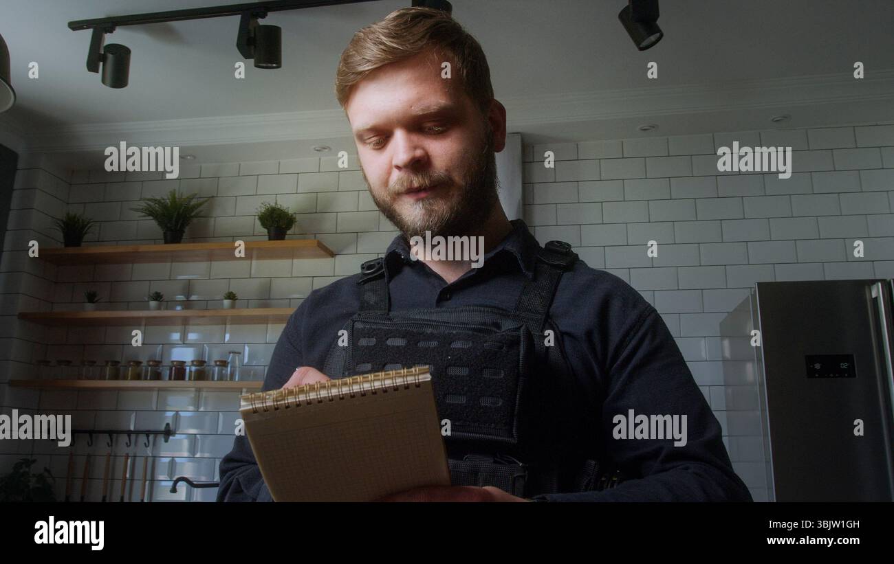 Bearded undercover police officer in tactical vest writing on clipboard ...