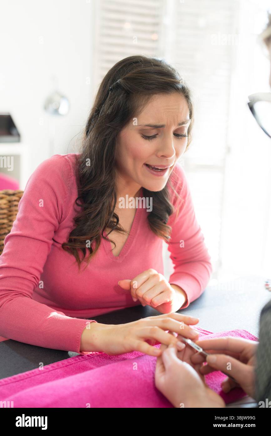 female customer expressing pain while having manicure Stock Photo - Alamy