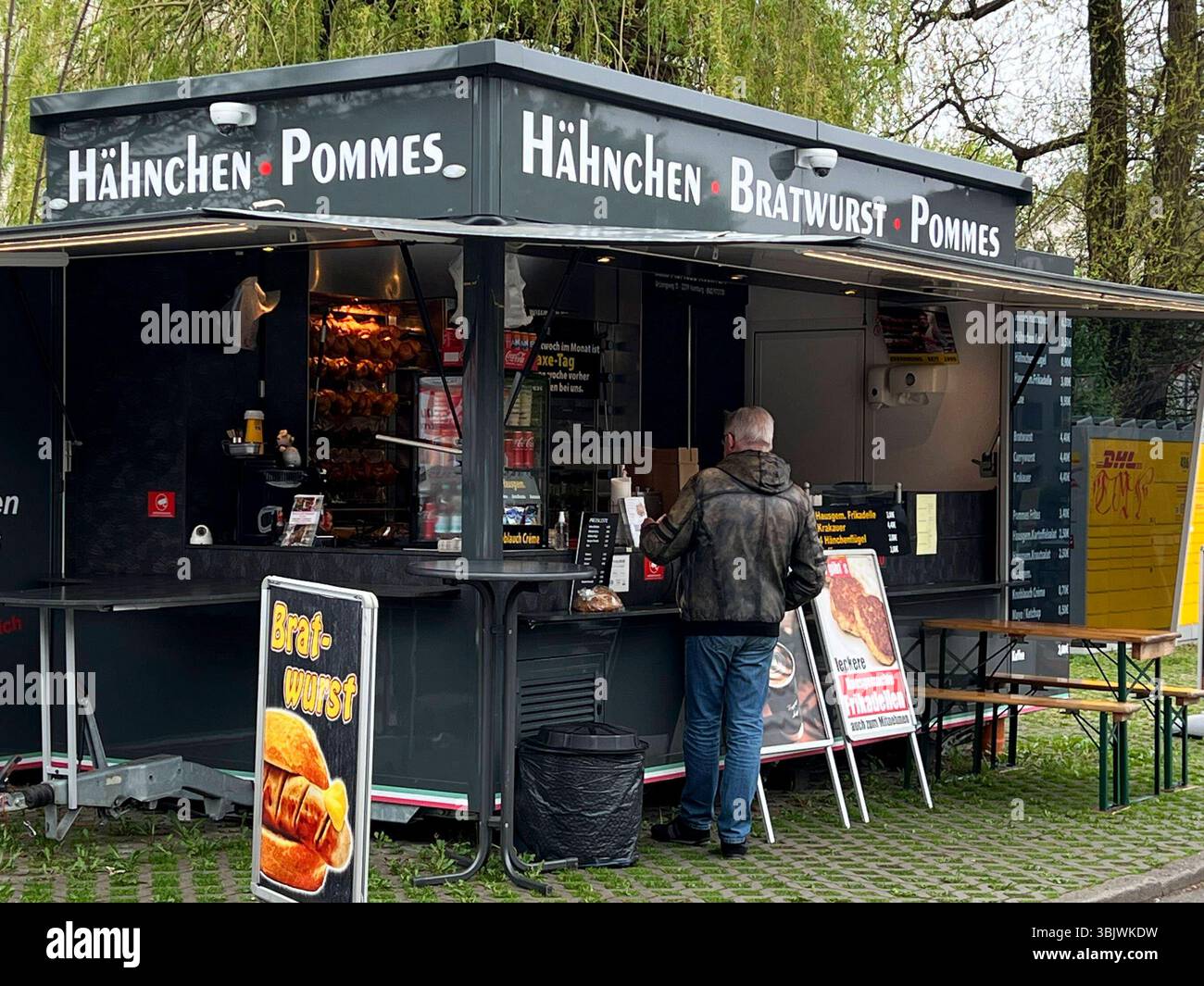 Imbisswagen mit Werbetafeln und stehtische steht auf einen Parkplatz ...