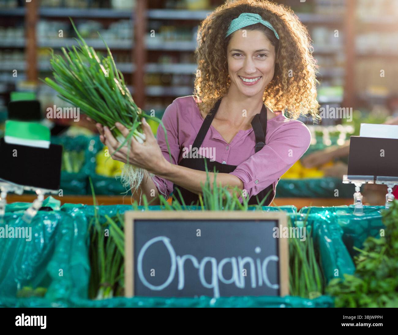 Female produce clerk wearing black apron smiling and holding green ...