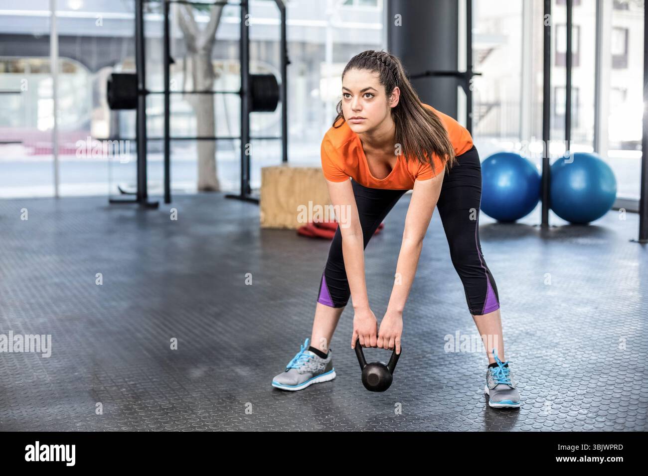 Woman in orange sports shirt lifting kettlebell in gym with weight ...