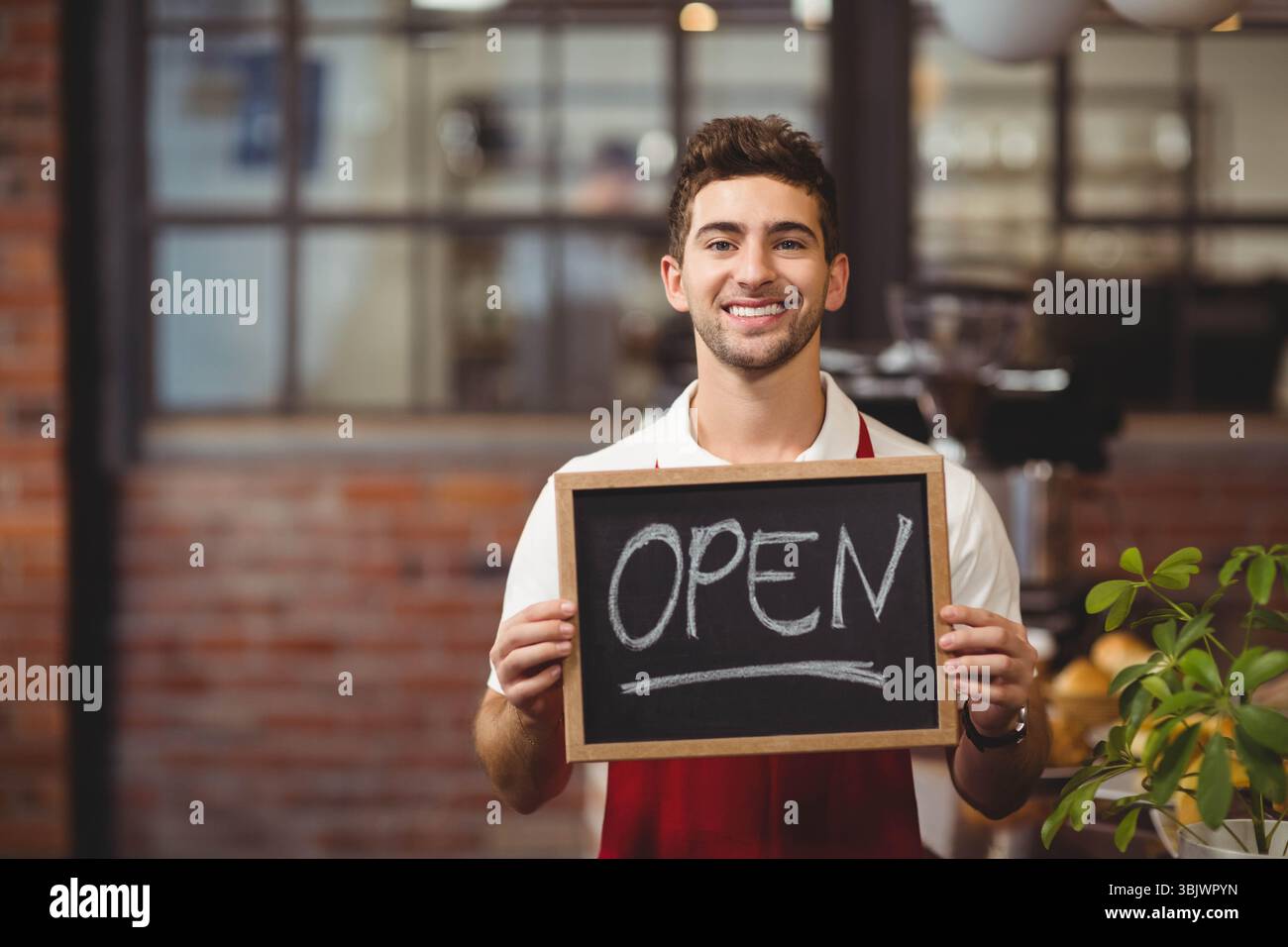 Barista wearing red apron is holding OPEN chalkboard sign in brick ...
