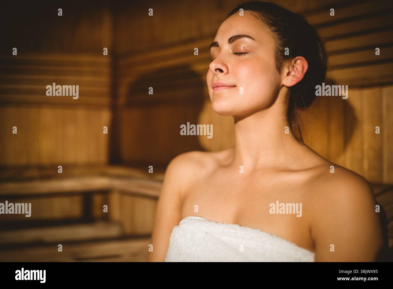 Spa guest sitting on wooden sauna bench soaking in warm golden light ...