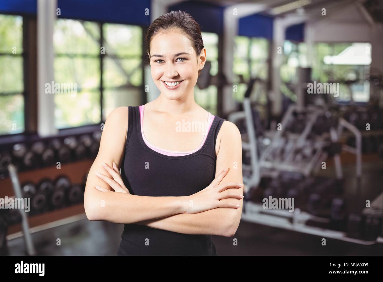 Woman standing with crossed arms in gym room with windows, showing ...