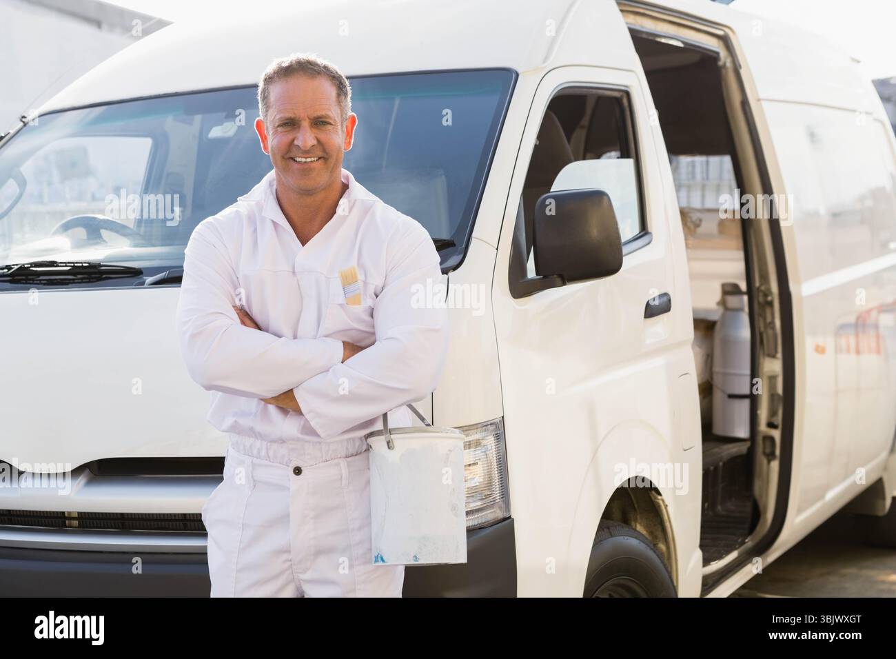 Middle-aged painter posing outside beside white van in overalls holding ...