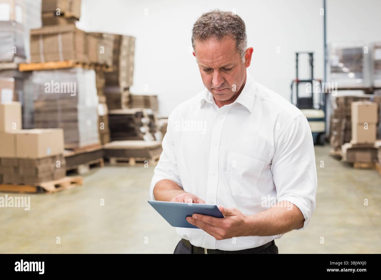 Mature adult man standing in warehouse checking tablet near forklift ...