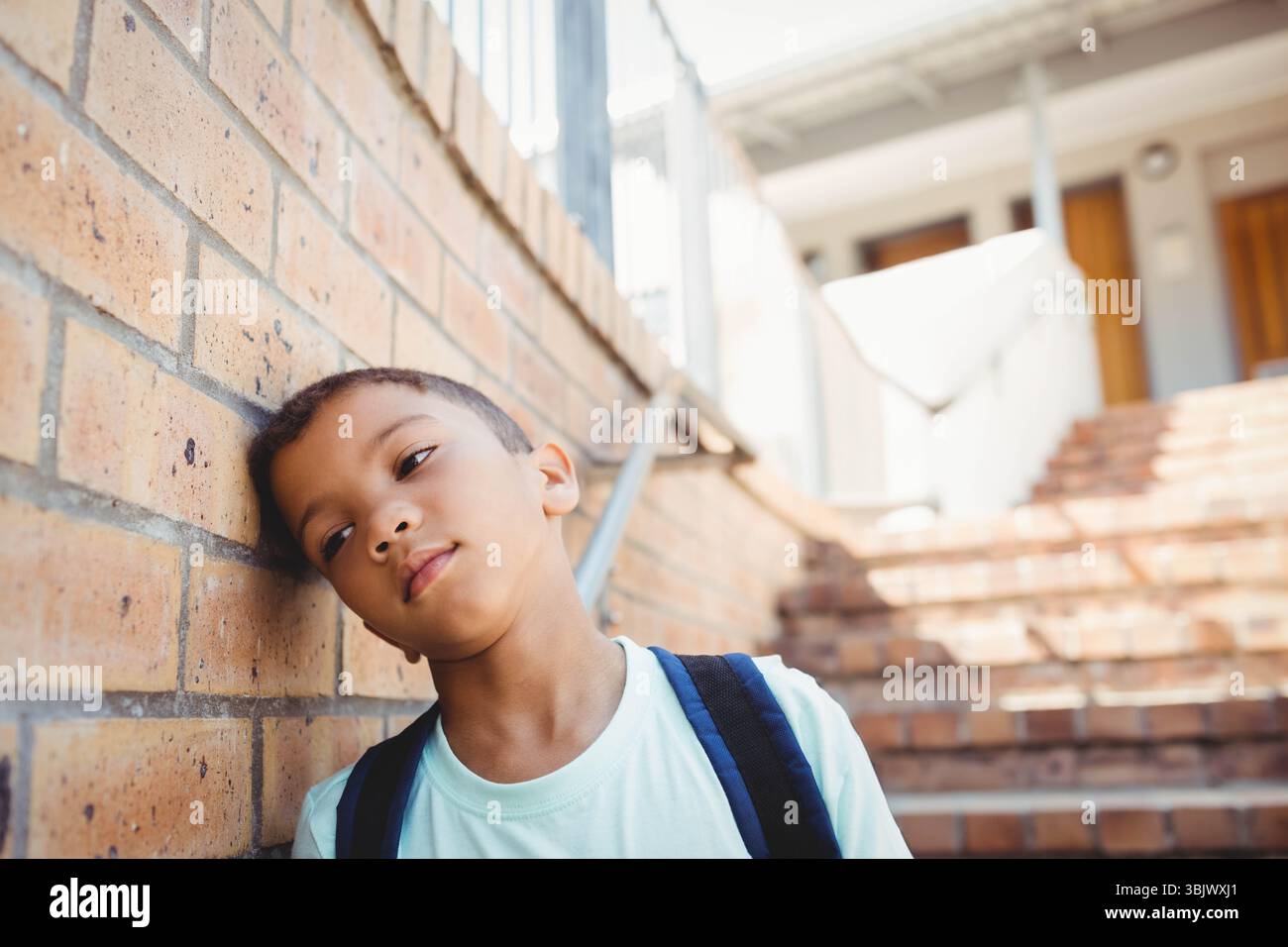 Boy student leaning head against tan brick wall at base of brick stairs ...