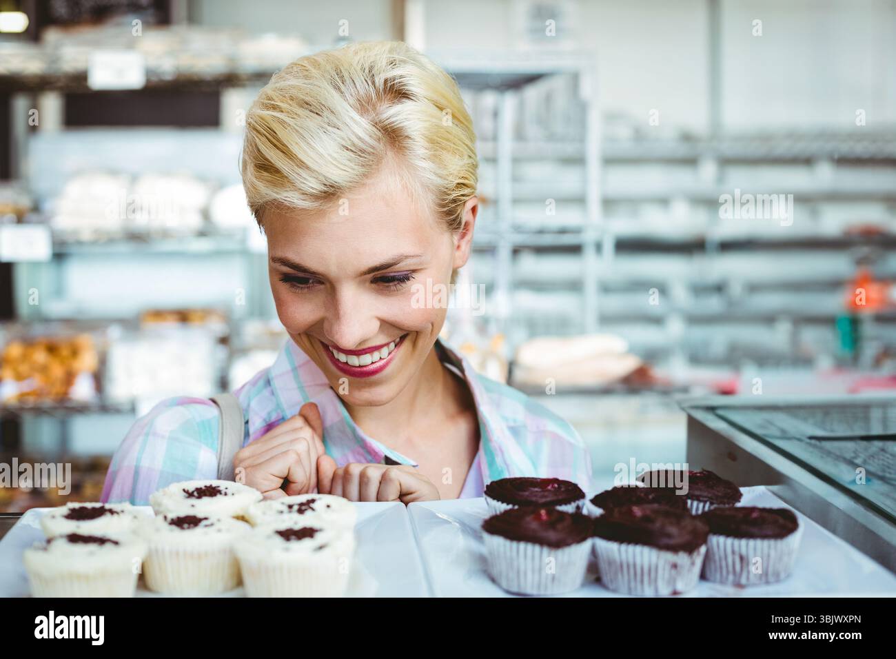 Woman in her twenties leaning over bakery display counter examining ...