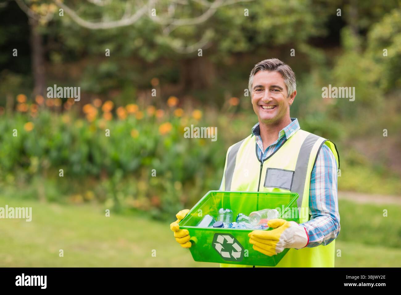 Male recycling worker smiling, holding green bin wearing yellow gloves ...