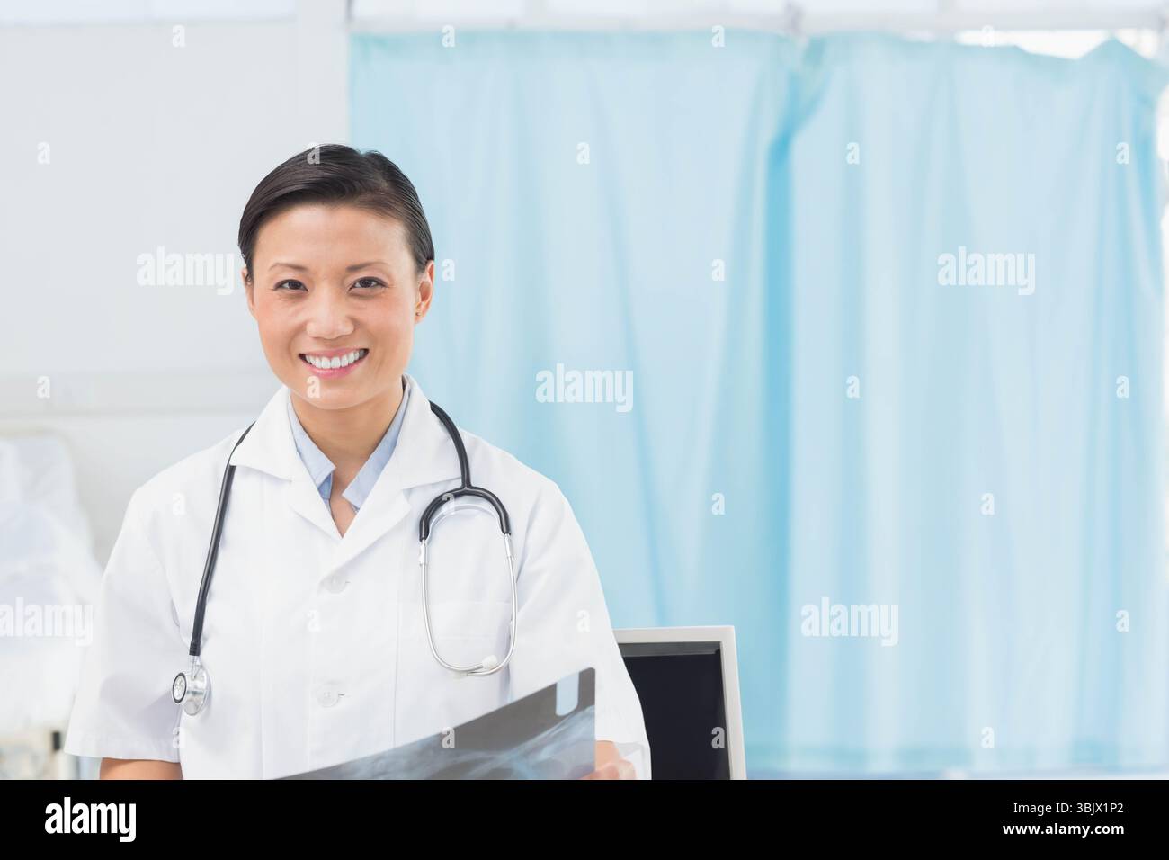 Doctor examining X-ray film in exam room with stethoscope, computer ...
