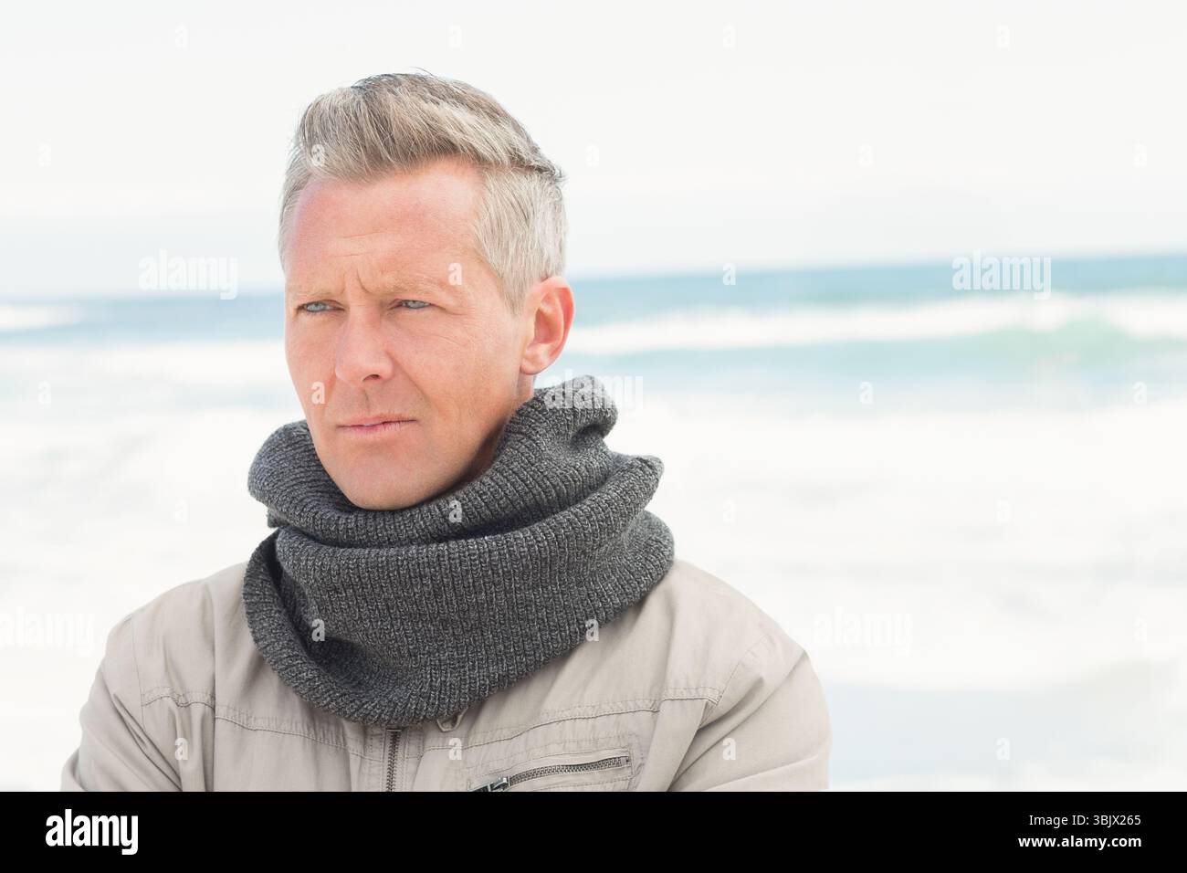 Man in early 50s standing on sandy beach wearing beige zip-up jacket ...