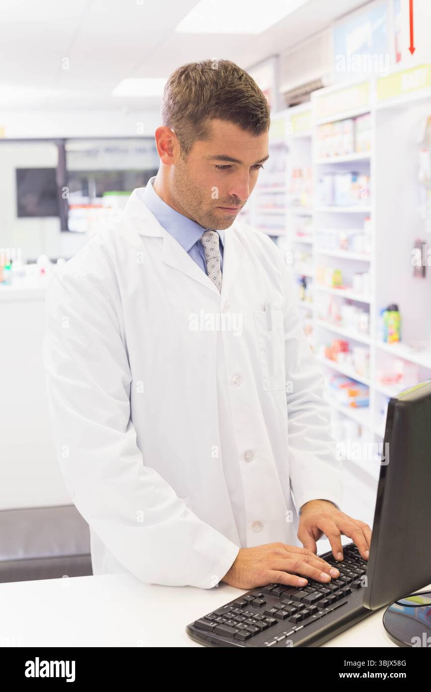 Mid adult male pharmacist typing on keyboard behind counter at pharmacy ...