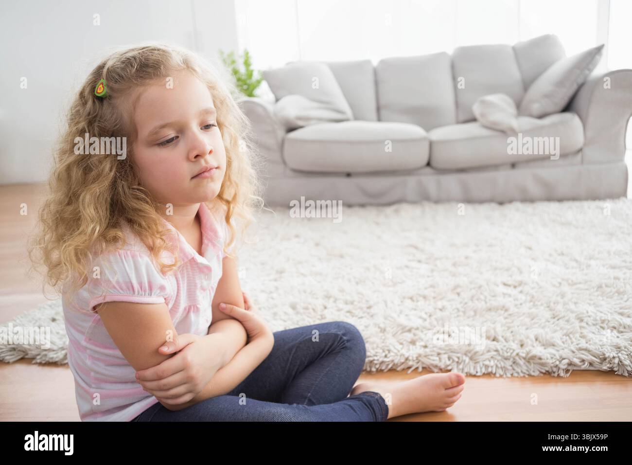 Female child sitting cross-legged on plush rug by sofa in living room ...