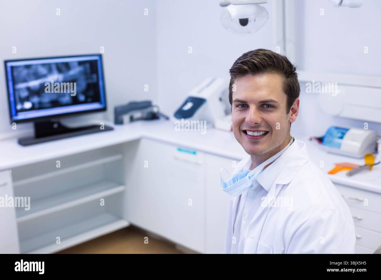 Male dentist standing by counter in treatment room with dental X-ray on ...